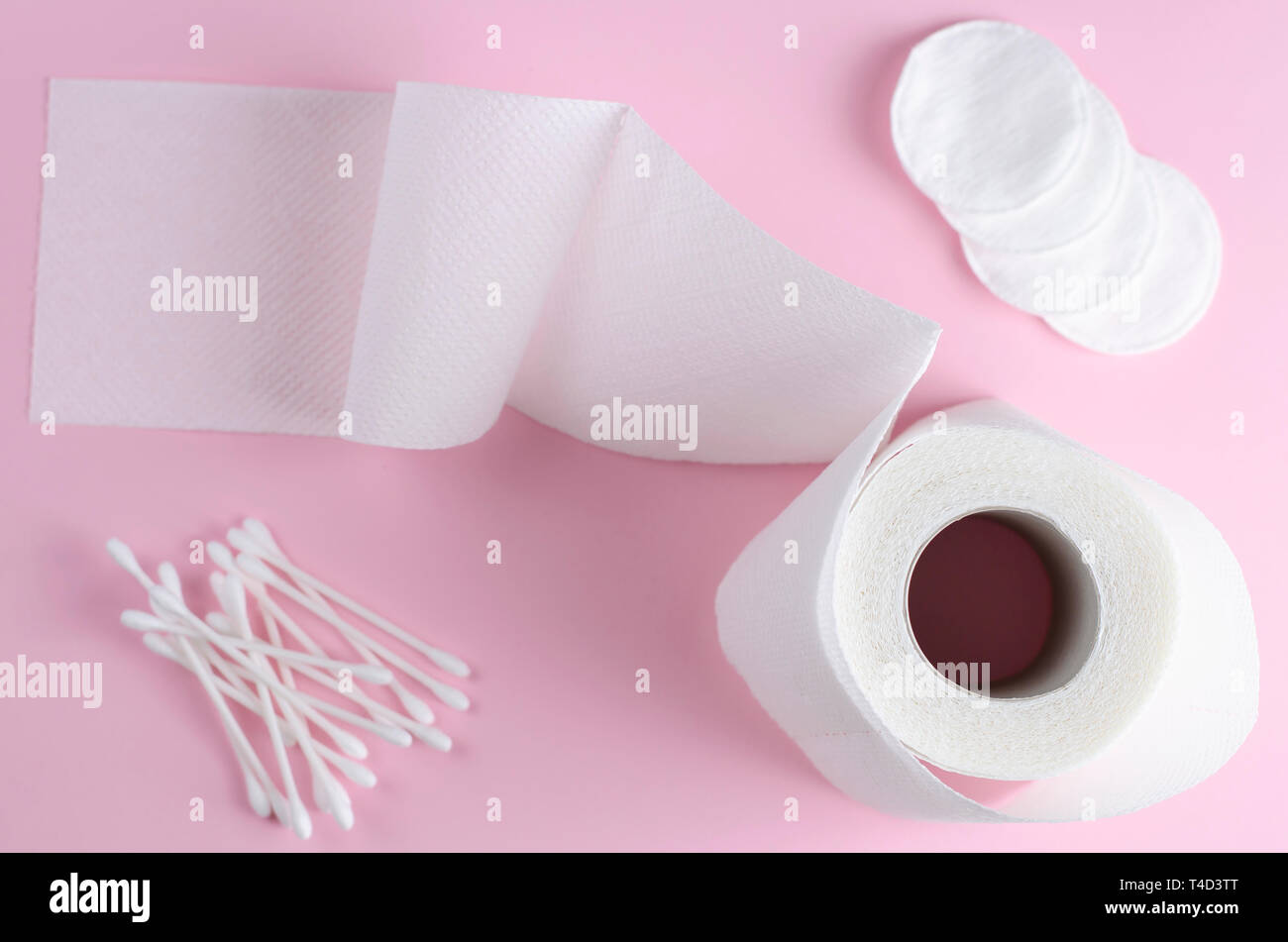 Ear sticks, cotton pads and toilet paper roll on pastel pink background ...
