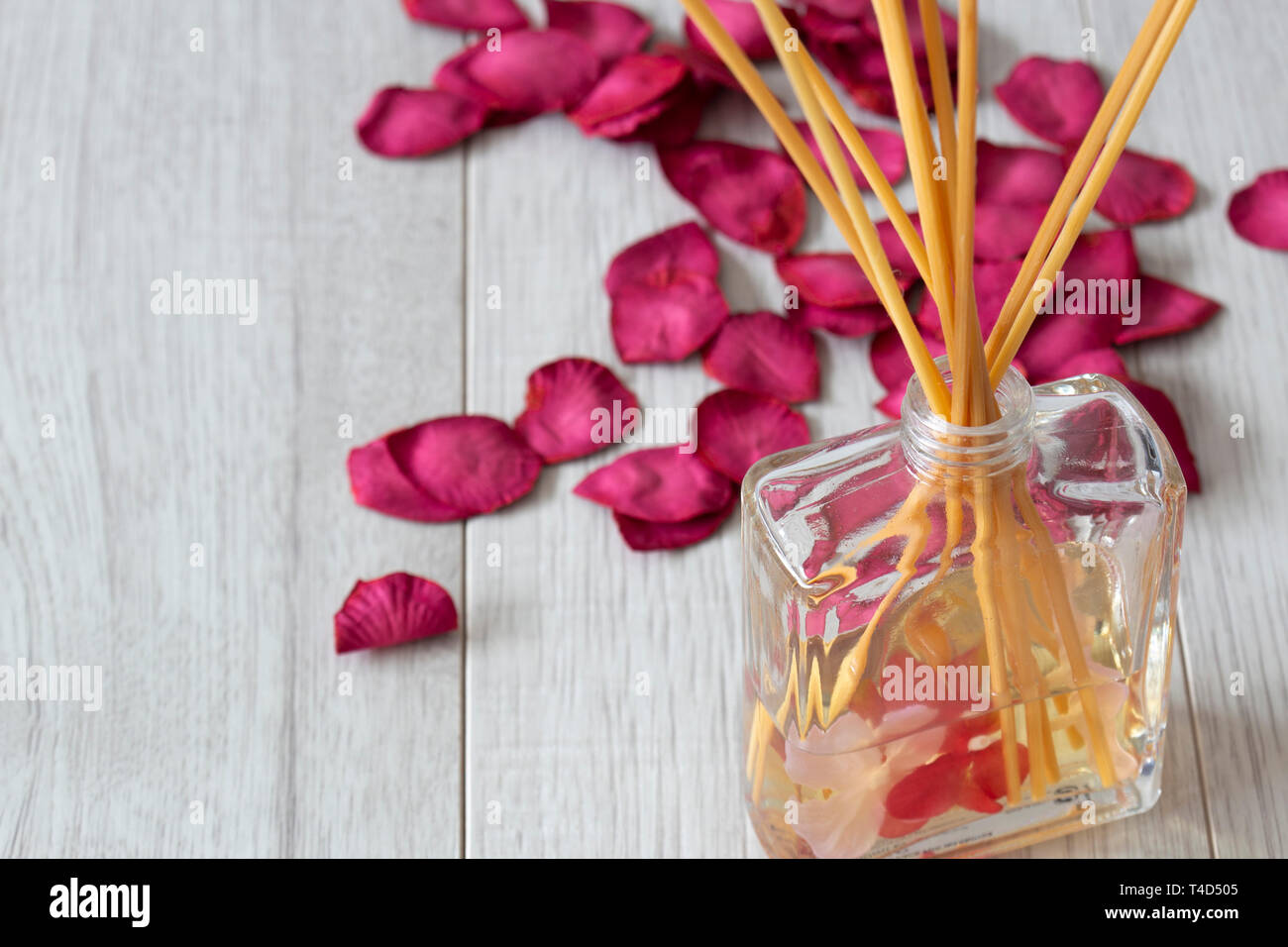 Reed diffuser with fragrance in a glass jar with rose petals on a grey ...