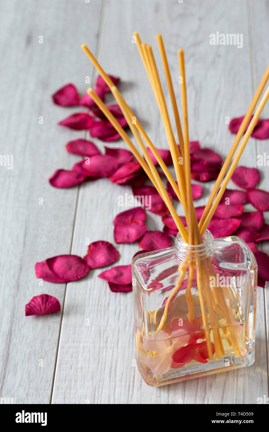 Reed diffuser with fragrance in a glass jar with rose petals on a grey ...