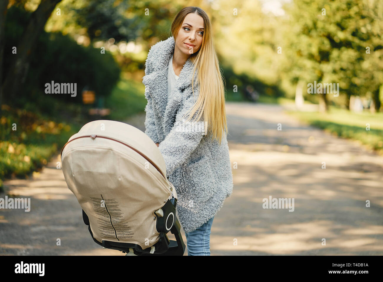 stylish young blonde mother pushing around a stroller with baby inside ...