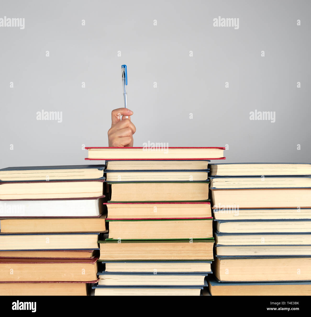 stack of different books on a gray background, hand sticks out from ...