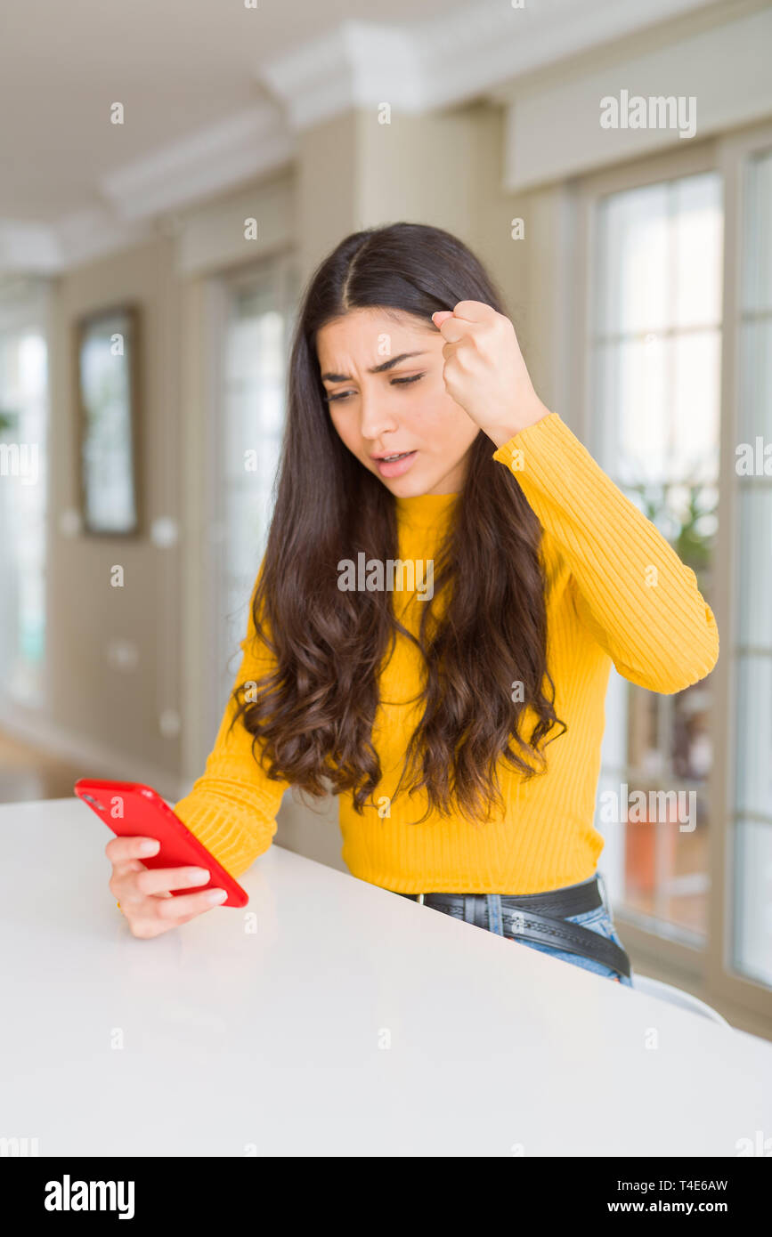 Young woman using red smartphone sending a message annoyed and ...