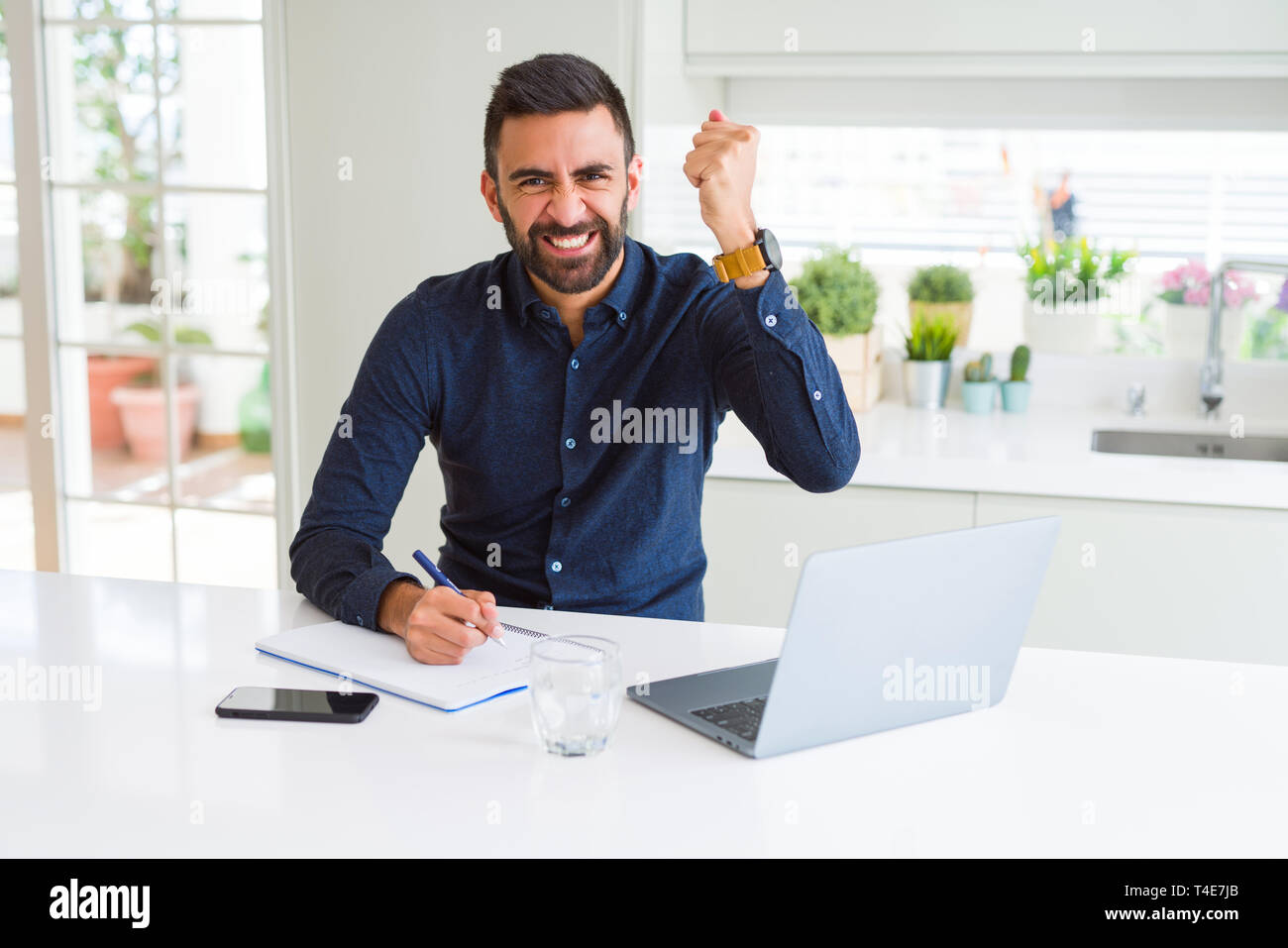 Handsome hispanic man working using computer and writing on a paper ...
