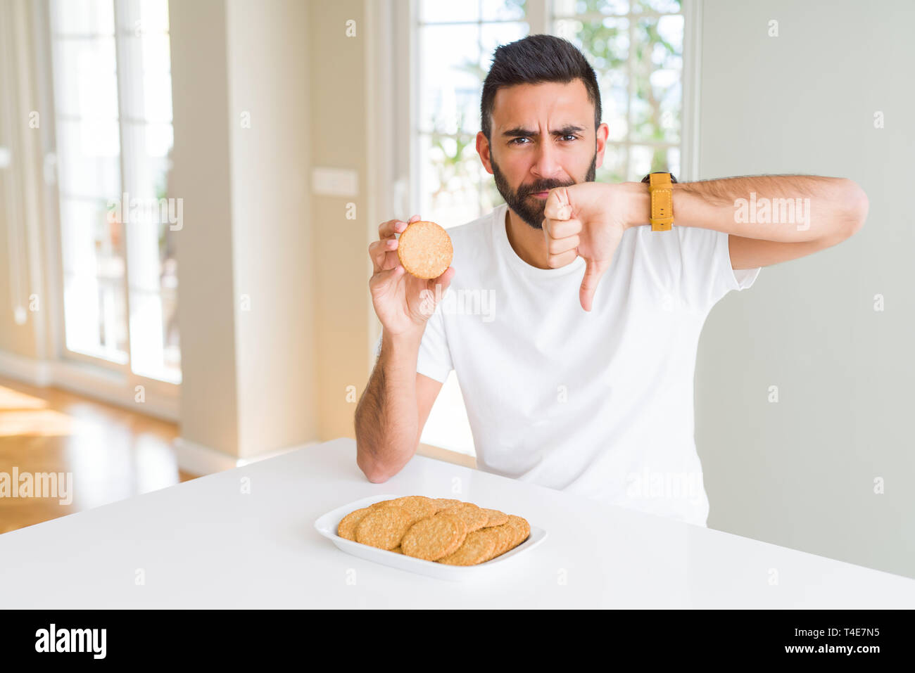 Handsome hispanic man eating healthy whole grain biscuits with angry ...