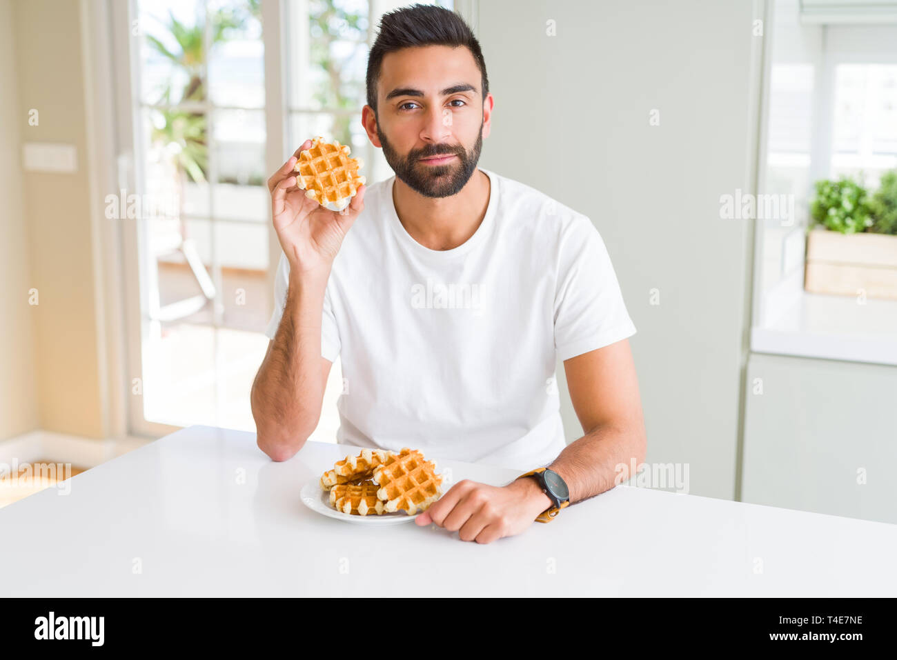 Handsome hispanic man eating sweet belgian waffle pastry with a ...