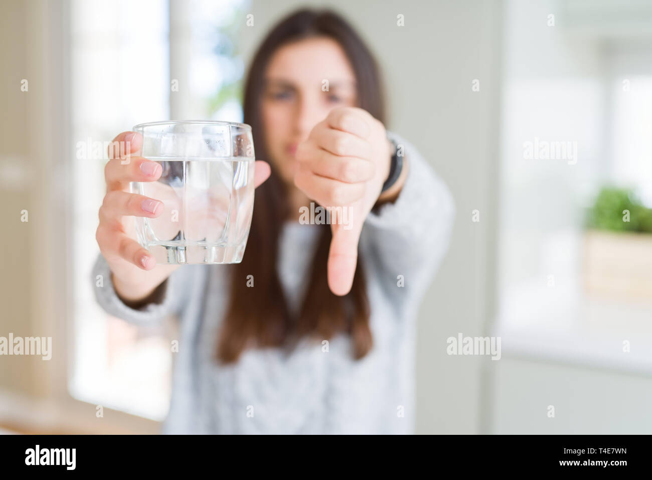 Beautiful young woman drinking a fresh glass of water with angry face ...