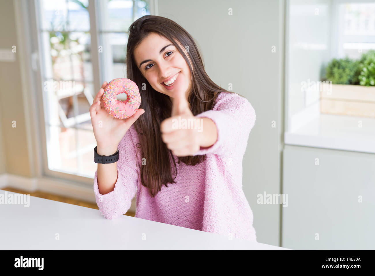 Beautiful young woman eating pink chocolate chips donut happy with big ...