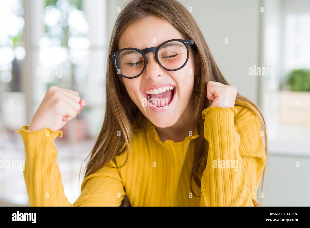 Beautiful young girl kid wearing glasses excited for success with arms ...