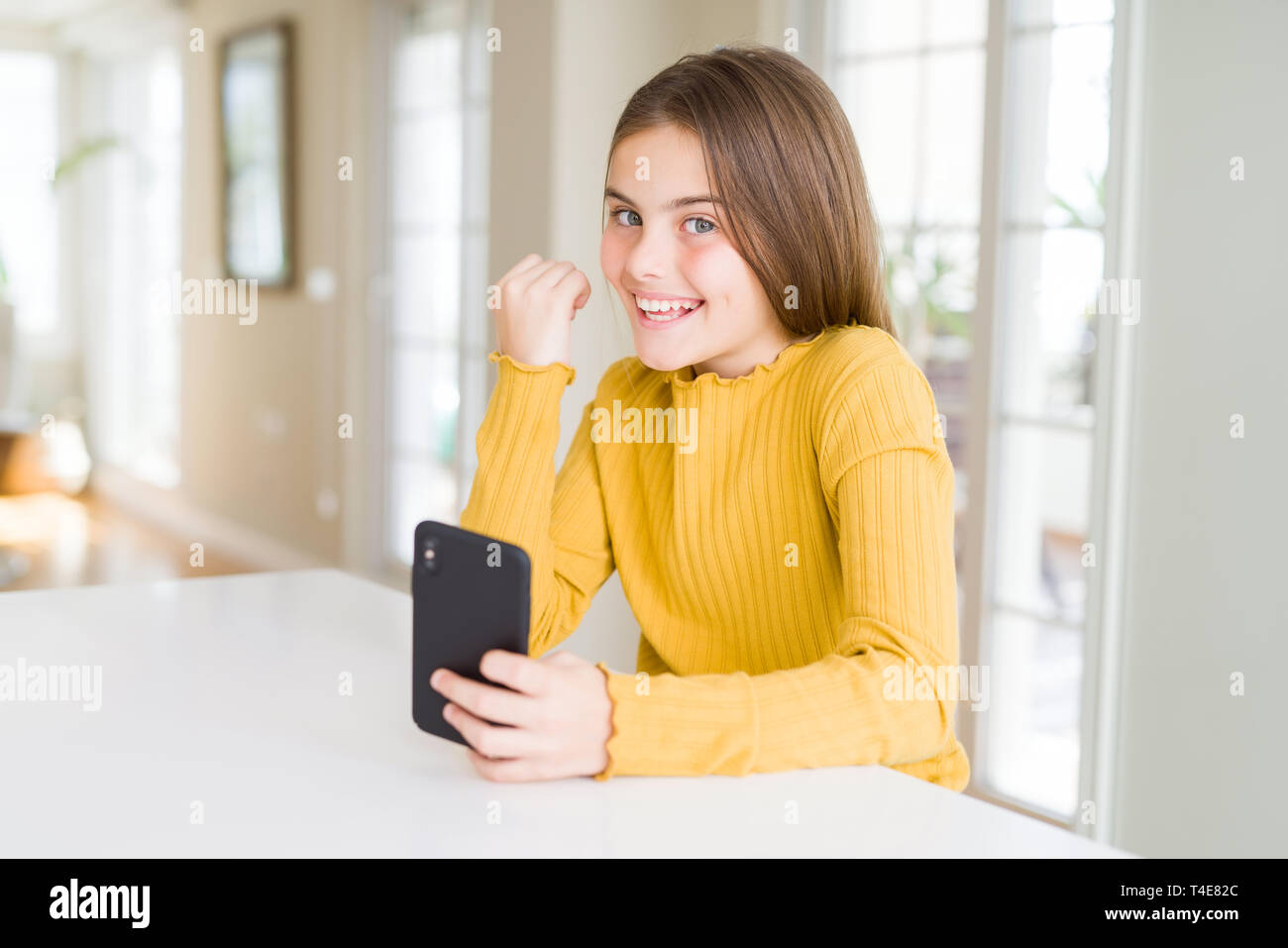 Beautiful young girl kid sending a message using smartphone pointing ...