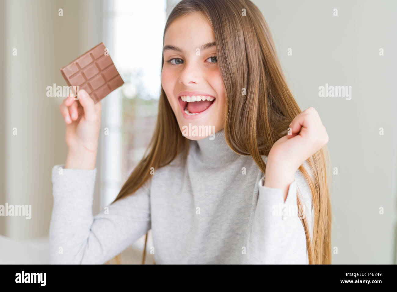 Beautiful young girl kid eating chocolate bar screaming proud and ...