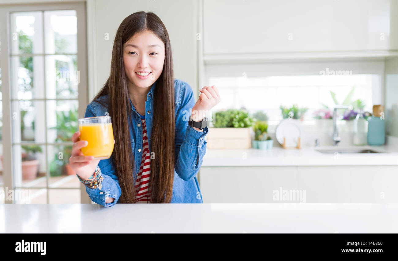 Beautiful Asian woman drinking a glass of fresh orange juice screaming ...
