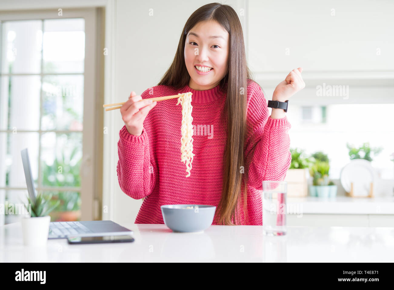 Beautiful Asian woman working using laptop and eating asian noodles ...