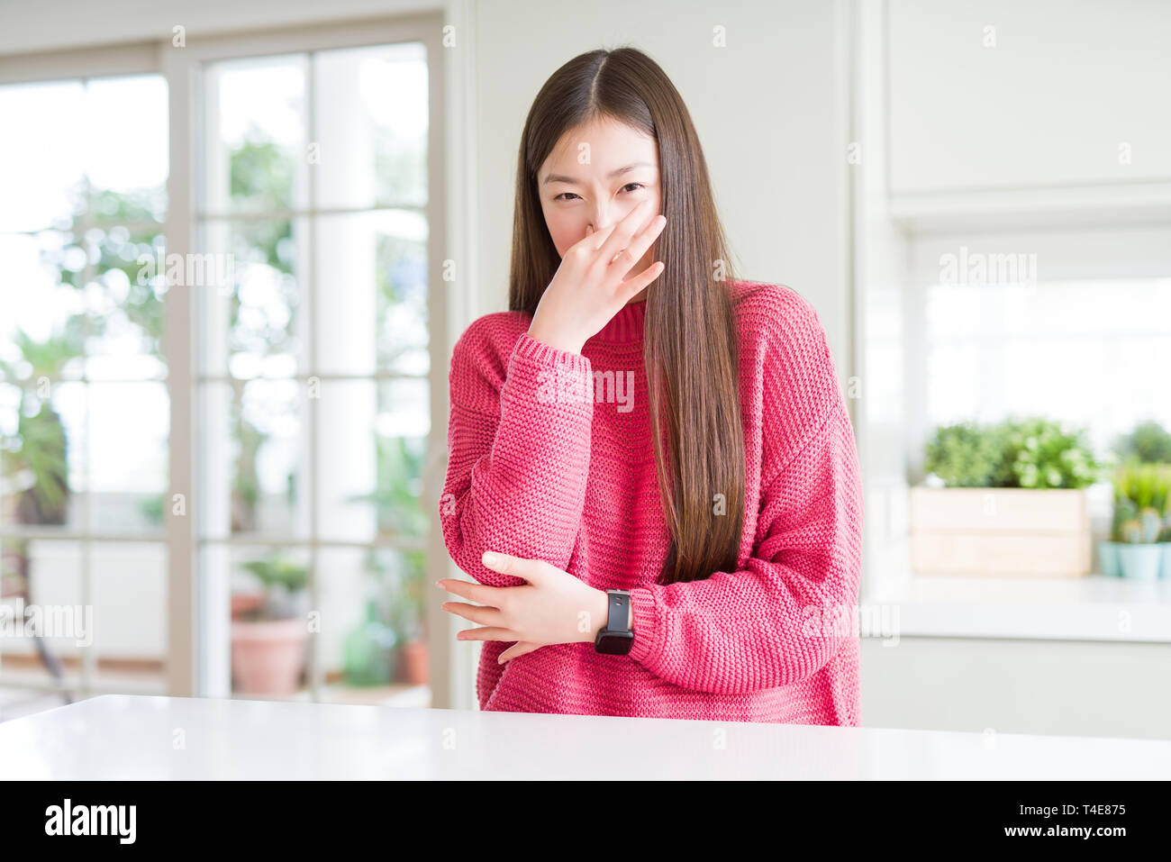 Beautiful Asian woman wearing pink sweater on white table smelling ...