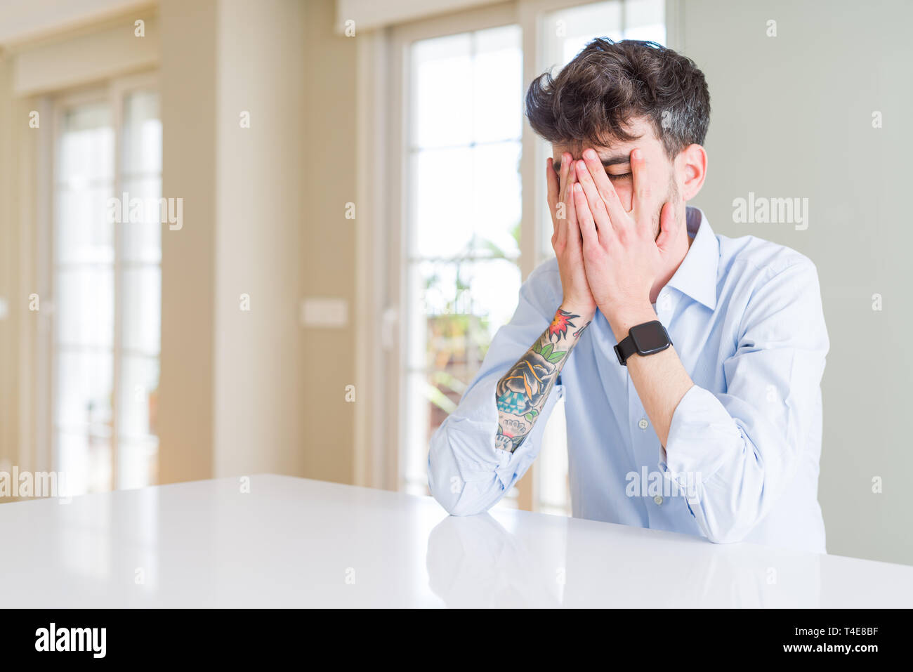 Young businesss man sitting on white table with sad expression covering ...