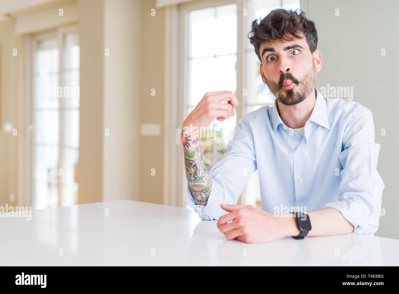 Young businesss man sitting on white table making fish face with lips ...