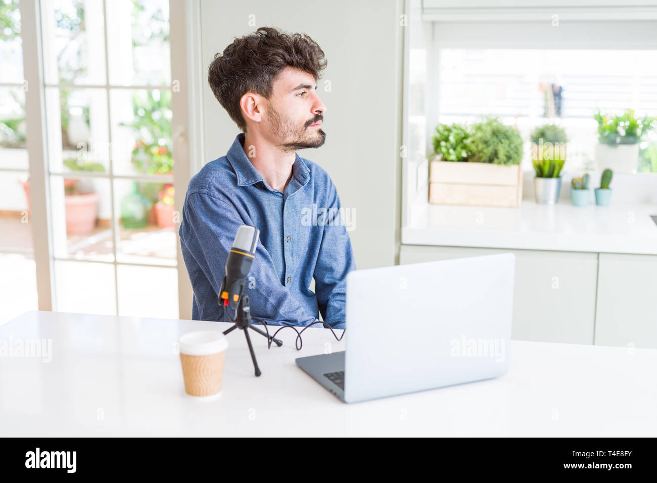 Young man recording podcast using microphone and laptop looking to side ...