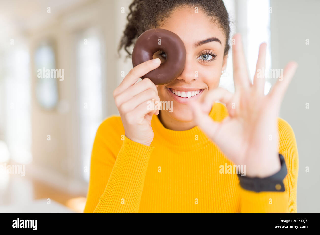 Young african american girl eating sweet chocolate donut doing ok sign ...
