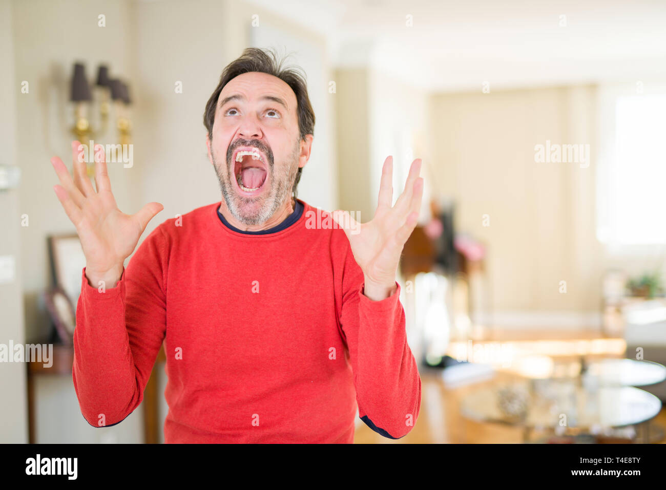 Handsome middle age man at home crazy and mad shouting and yelling with ...