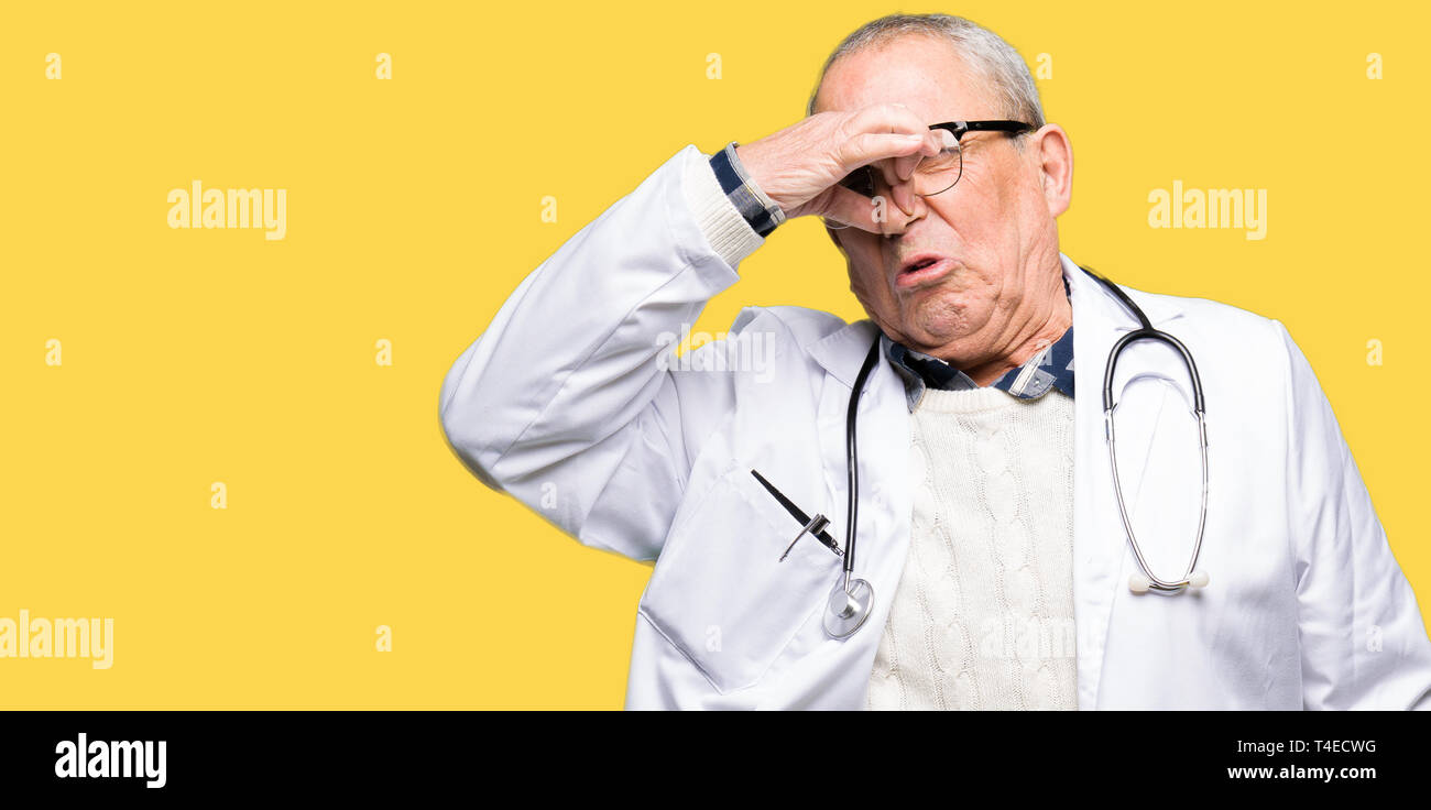Handsome senior doctor man wearing medical coat smelling something ...