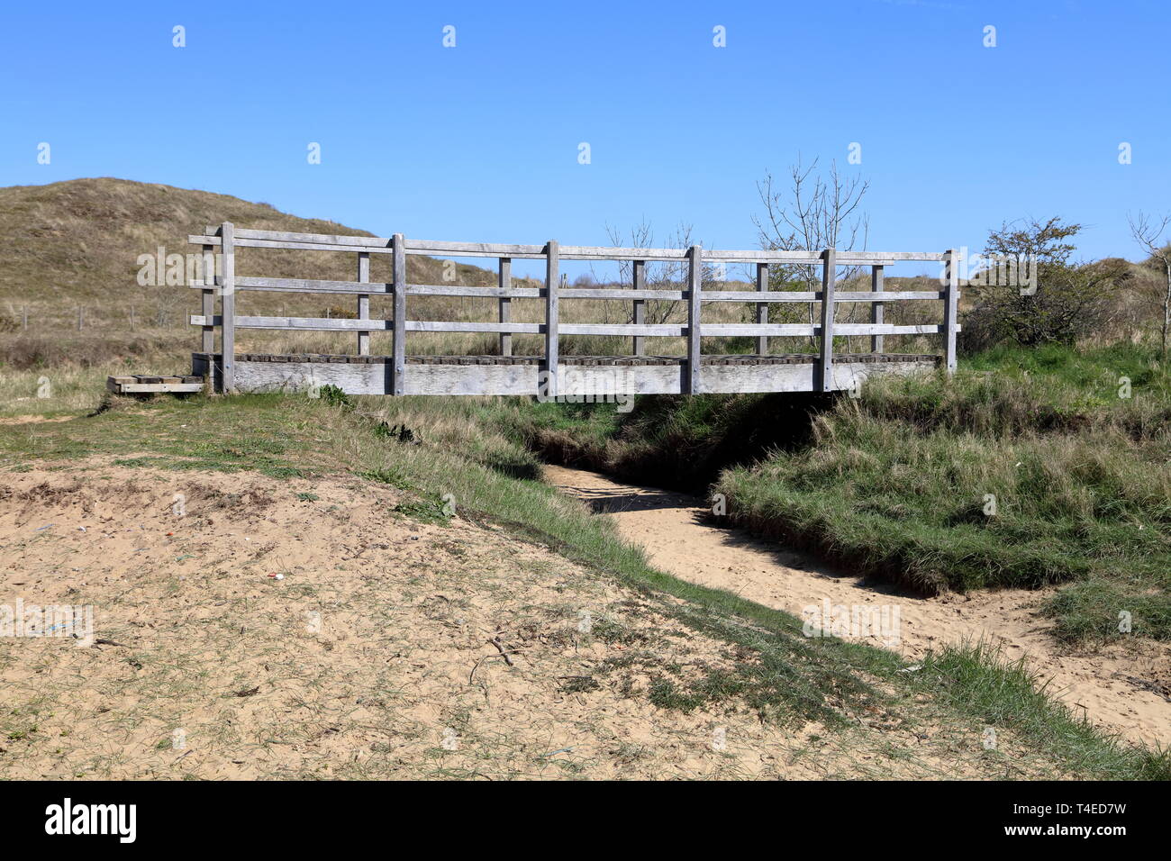 A fairly large wooden footbridge crossing a dried up sandy bottomed ...
