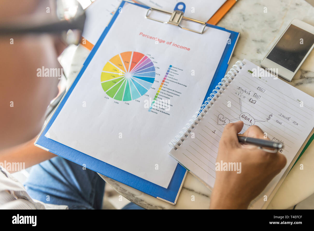 Rear view of man reading data and writing notes Stock Photo - Alamy
