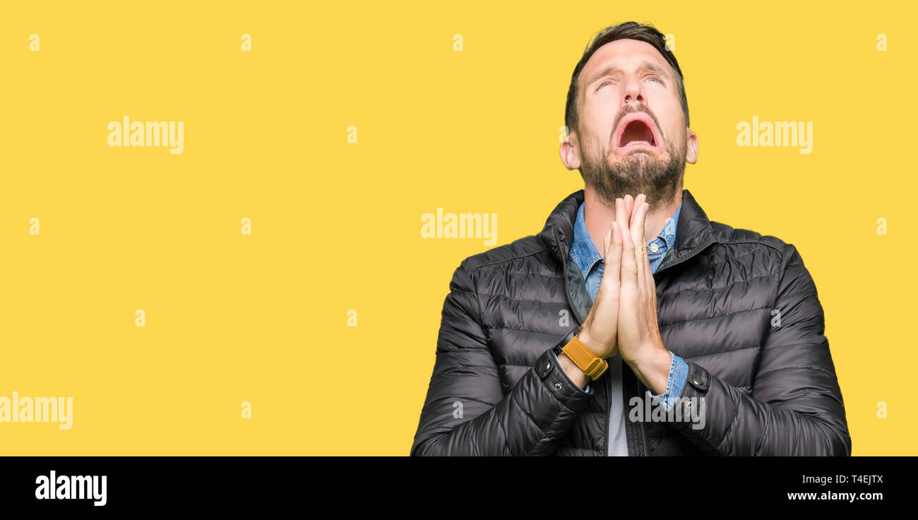 Handsome man wearing winter coat begging and praying with hands ...