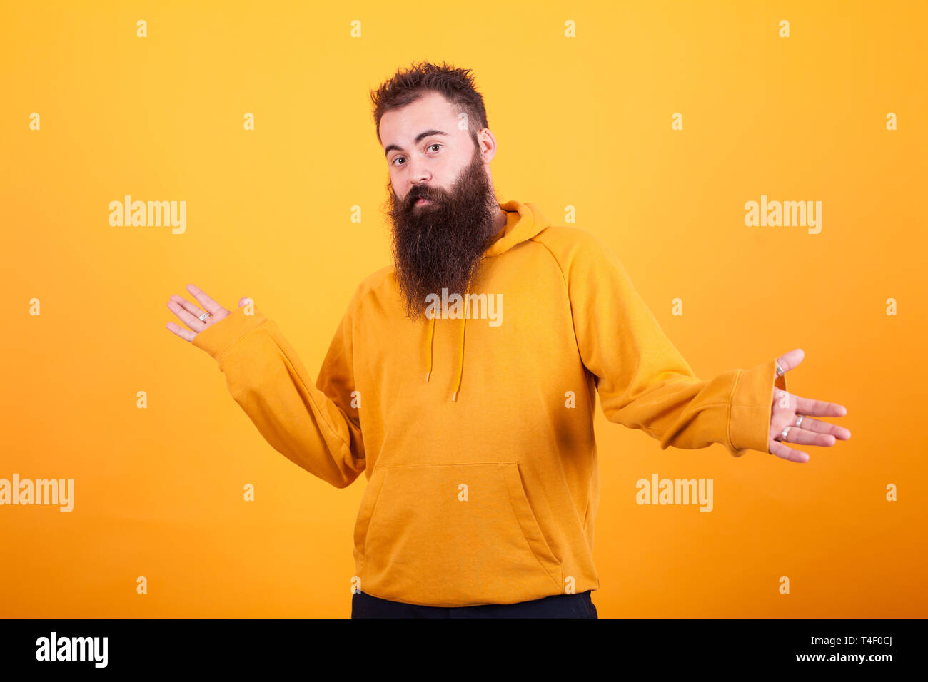 Handsome bearded man with orange hoodie looking confused. over yellow ...