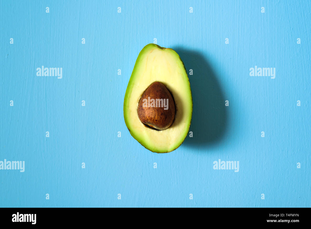 Avocado half on light blue background. Central conposition, hard light ...