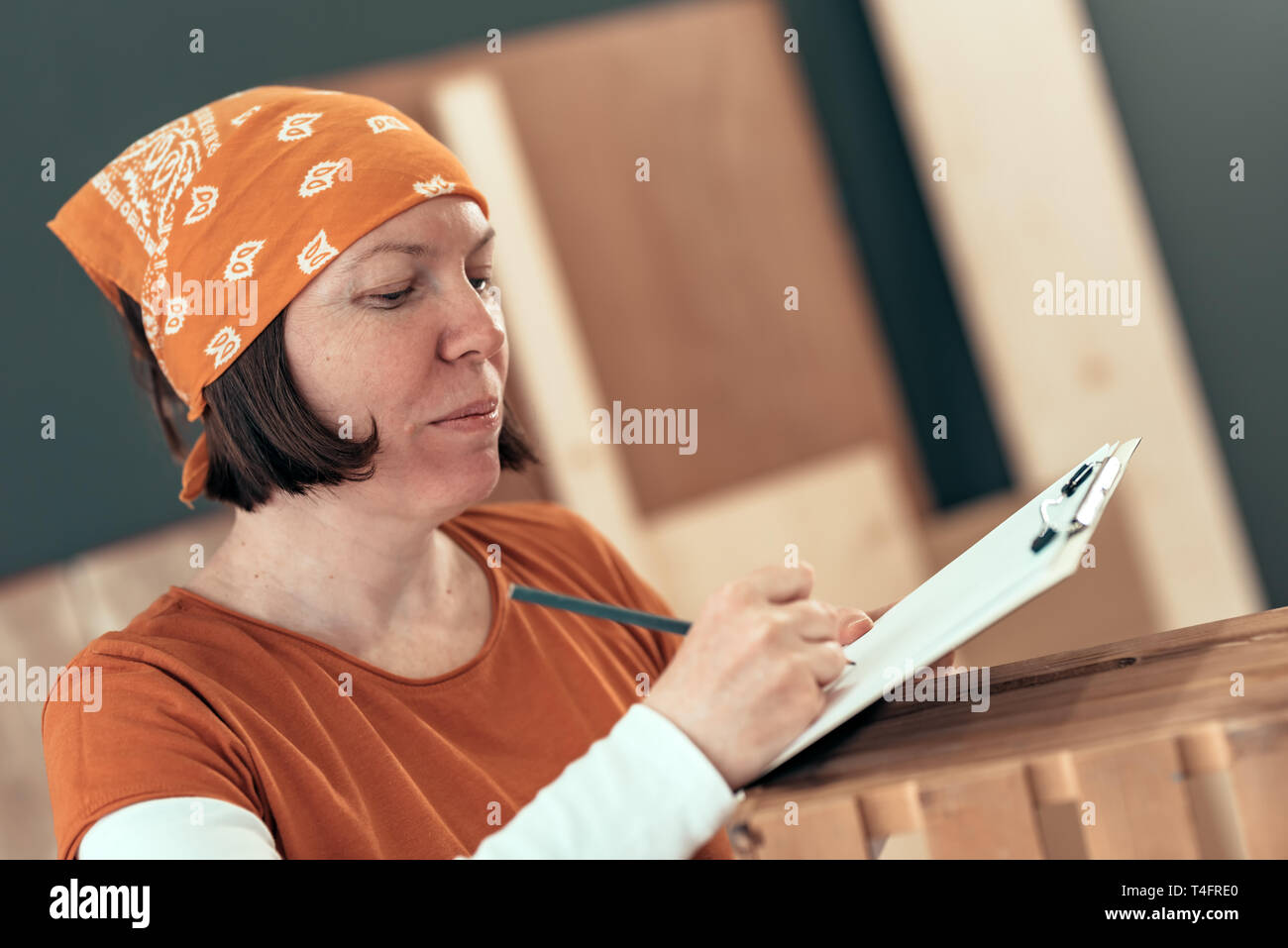Female carpenter writing DIY project notes after finishing wooden crate ...
