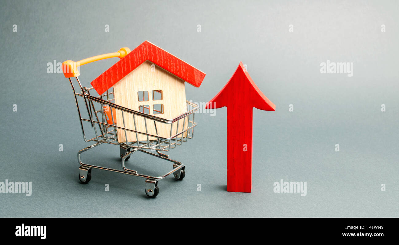 Wooden house in a supermarket trolley and red arrow up. The concept of ...