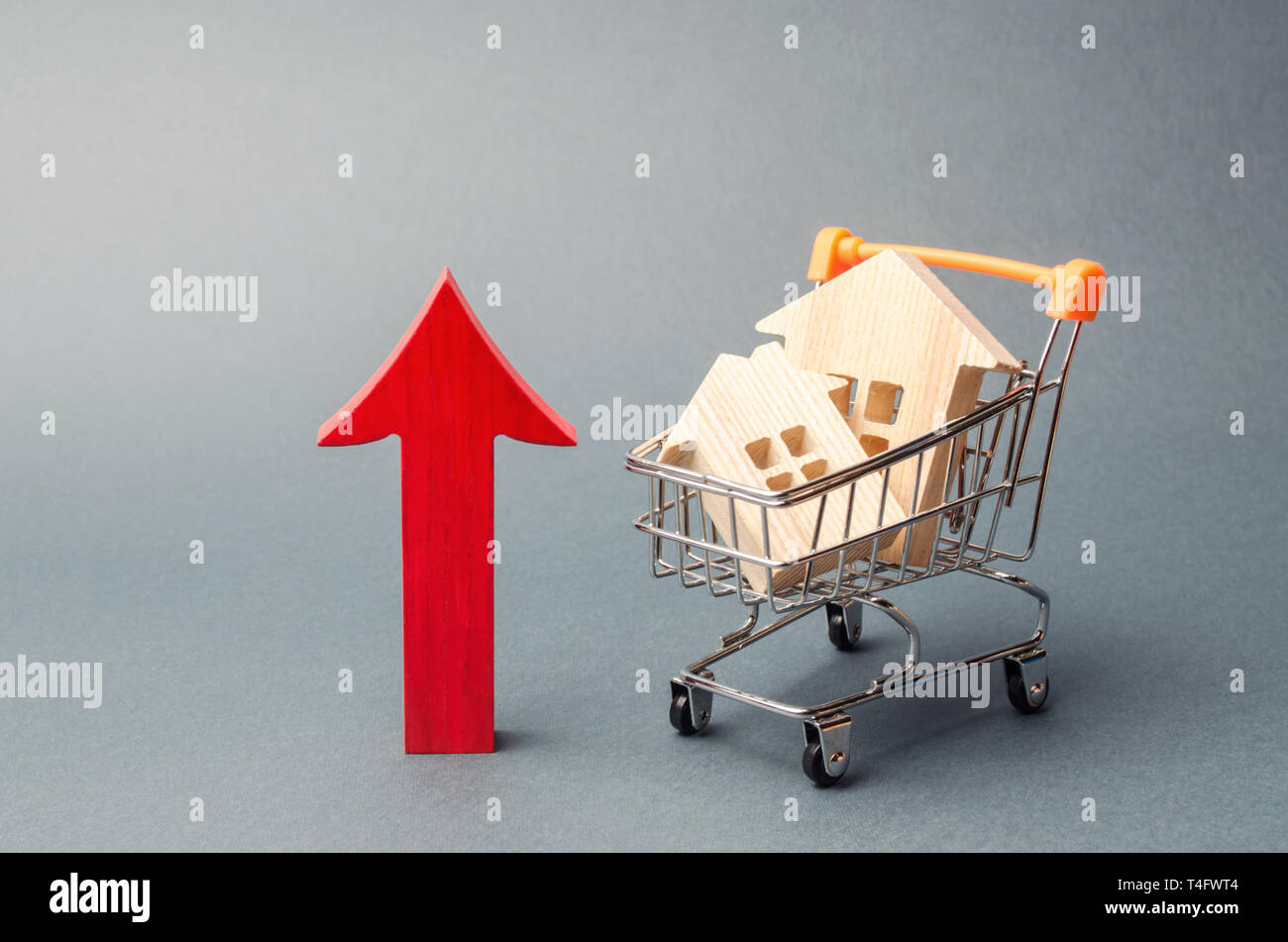 Wooden houses in a supermarket trolley and red arrow up. The concept of ...