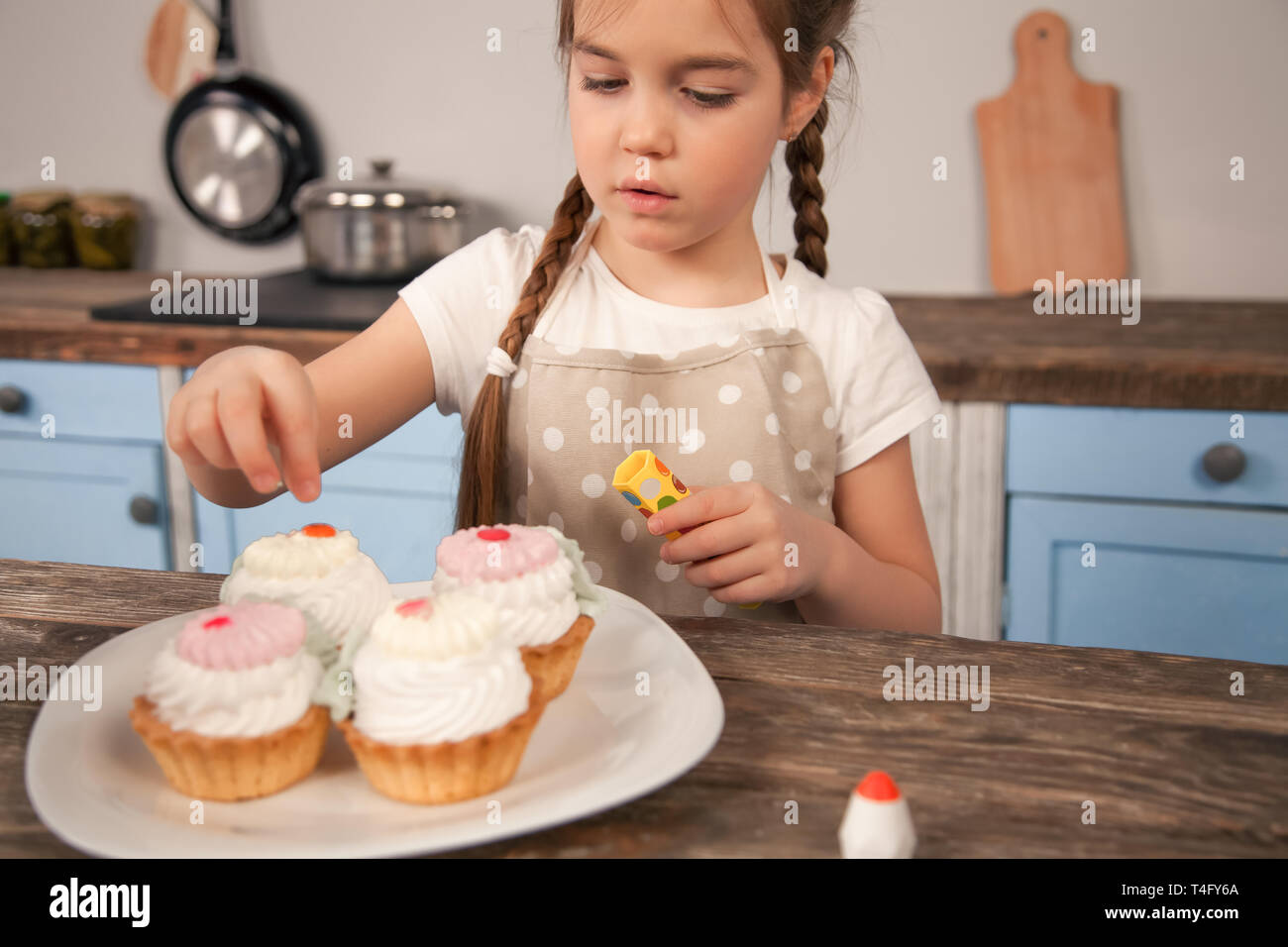 child daughter in the kitchen decorating cakes she is made with her mom ...