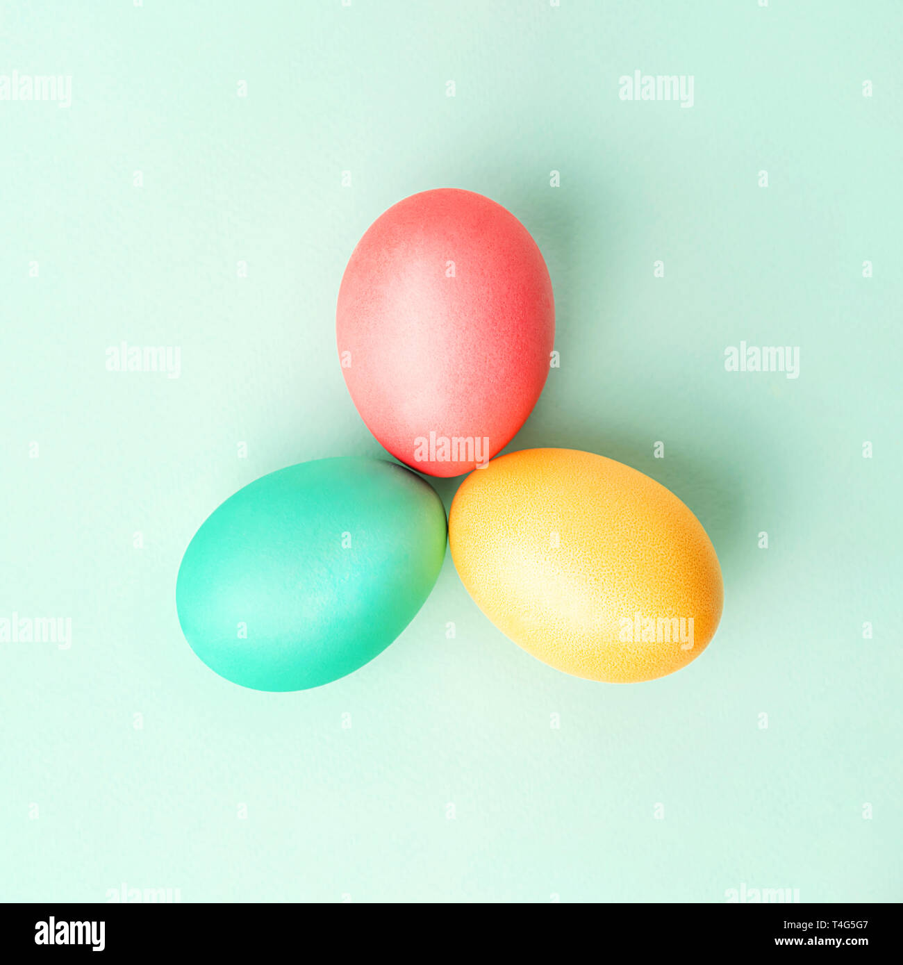 Three colorful handmade Easter eggs in triangle on mint colored ...