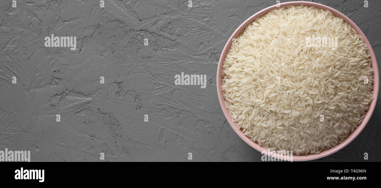 Dry white rice basmati in a pink bowl over gray surface, top view. Flat ...
