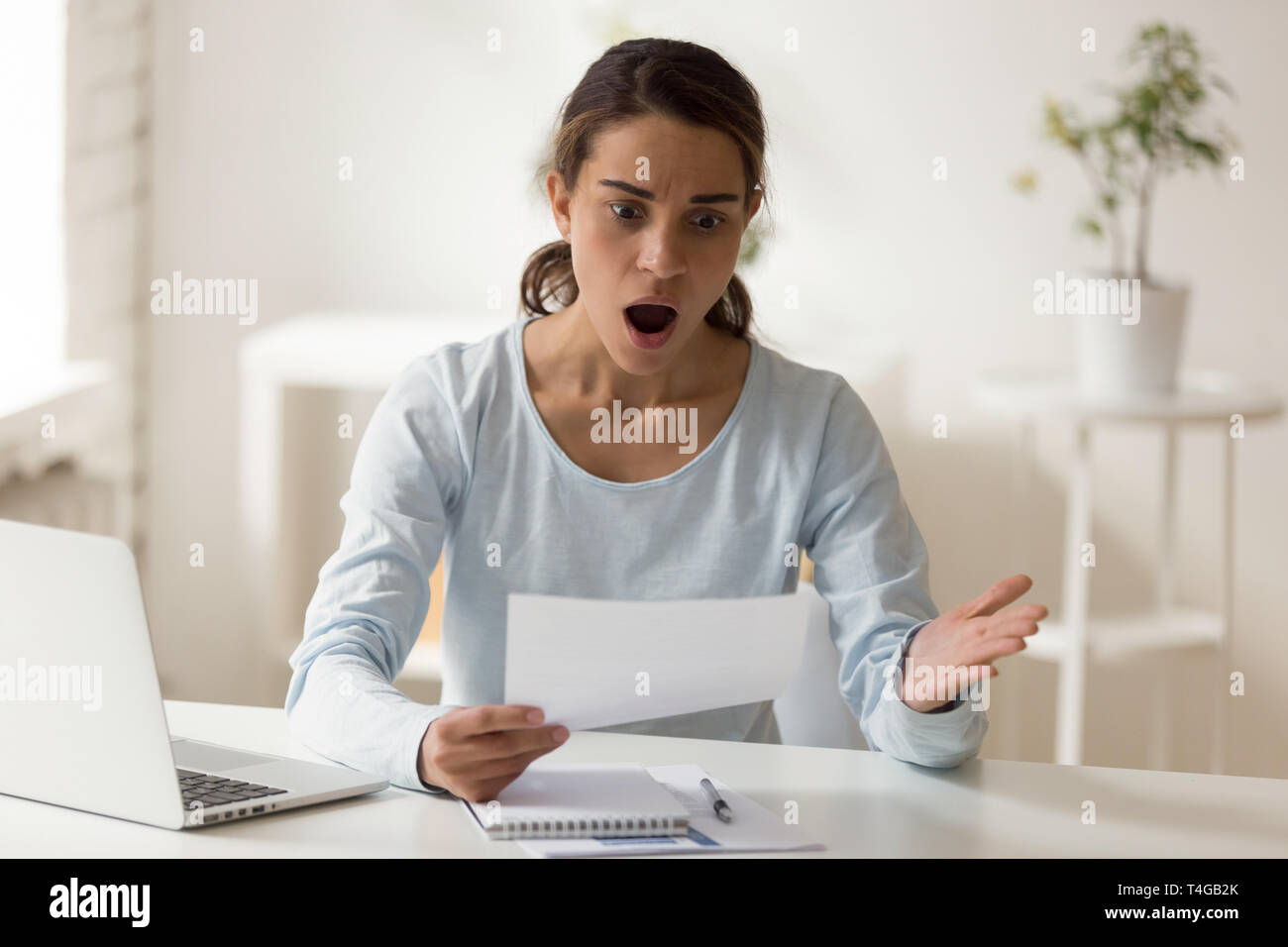 Shocked and confused woman looking at paper at desktop Stock Photo - Alamy