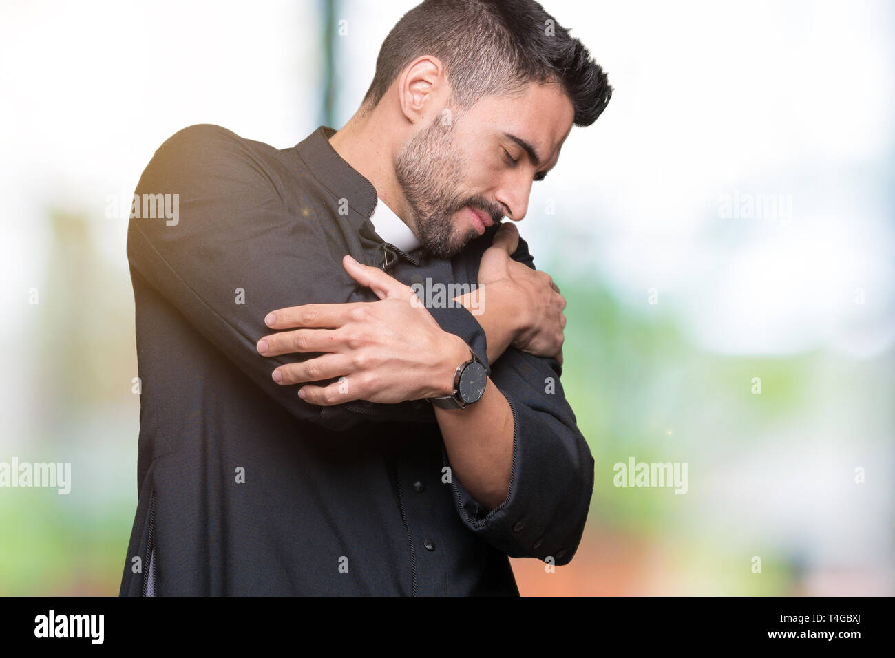 Young Christian priest over isolated background Hugging oneself happy ...