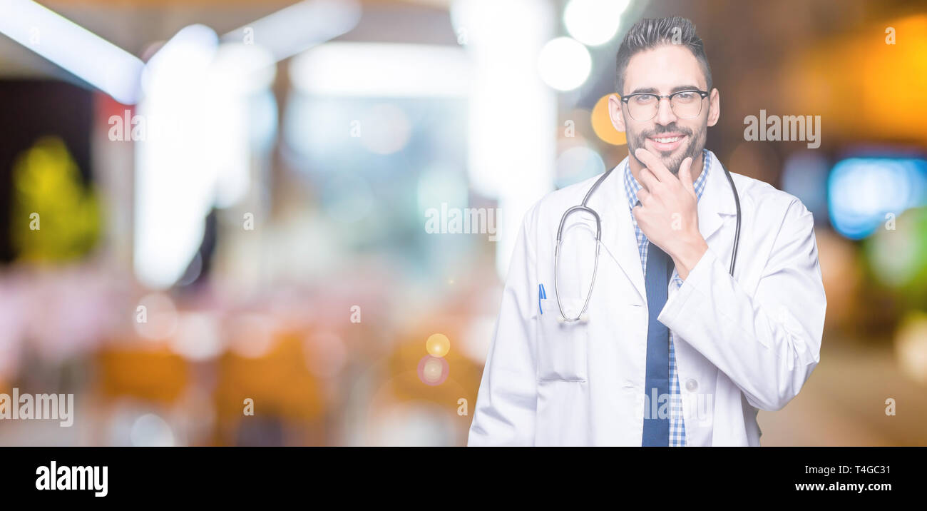 Handsome young doctor man over isolated background looking confident at ...