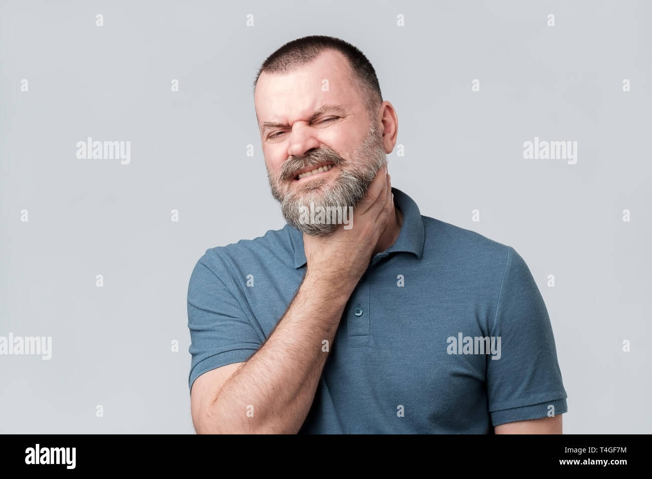 Sick man with beard with pain in throat on gray background. Studio shot ...
