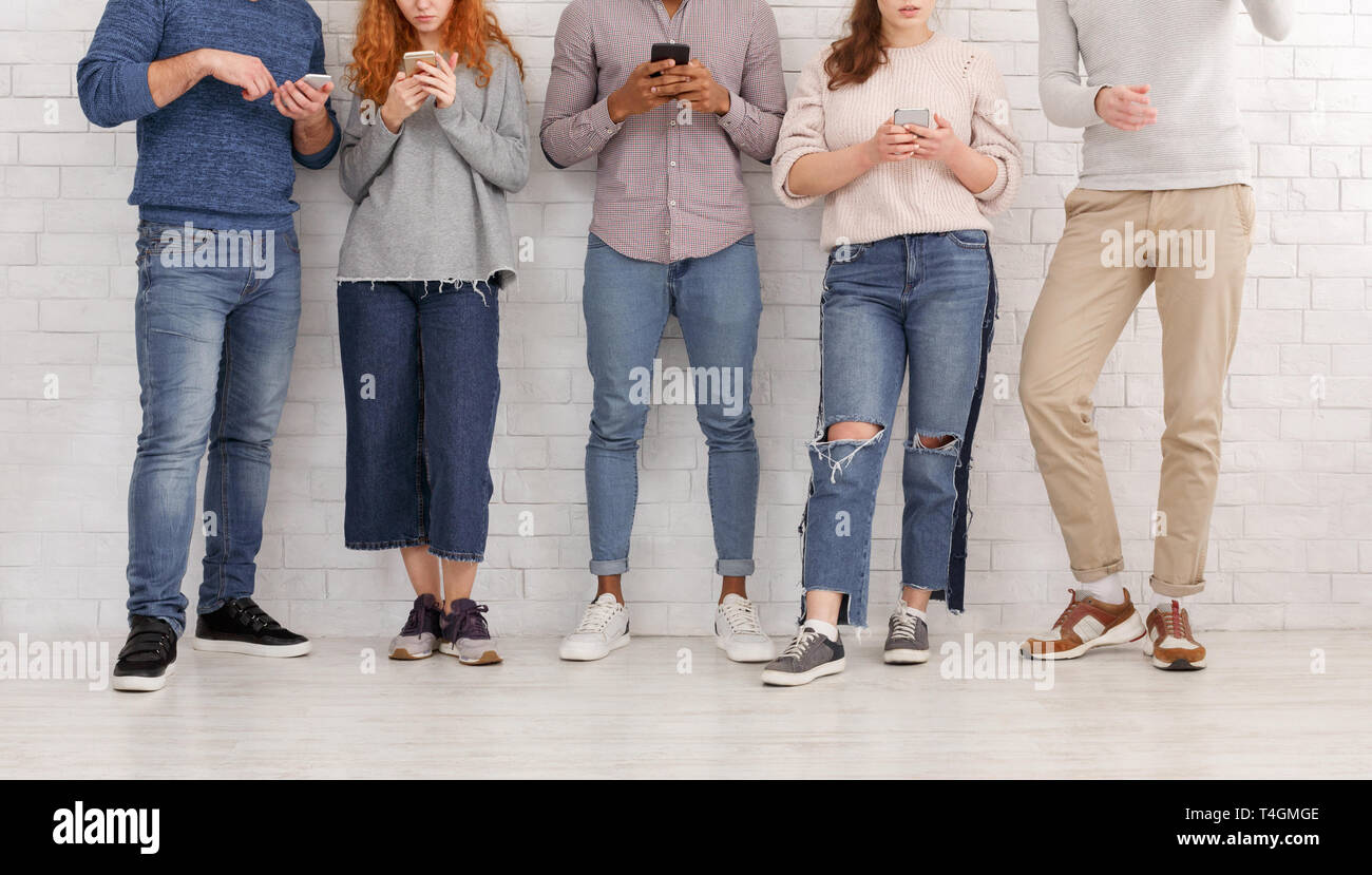 Young people texting on their smartphones, leaning on wall Stock Photo ...