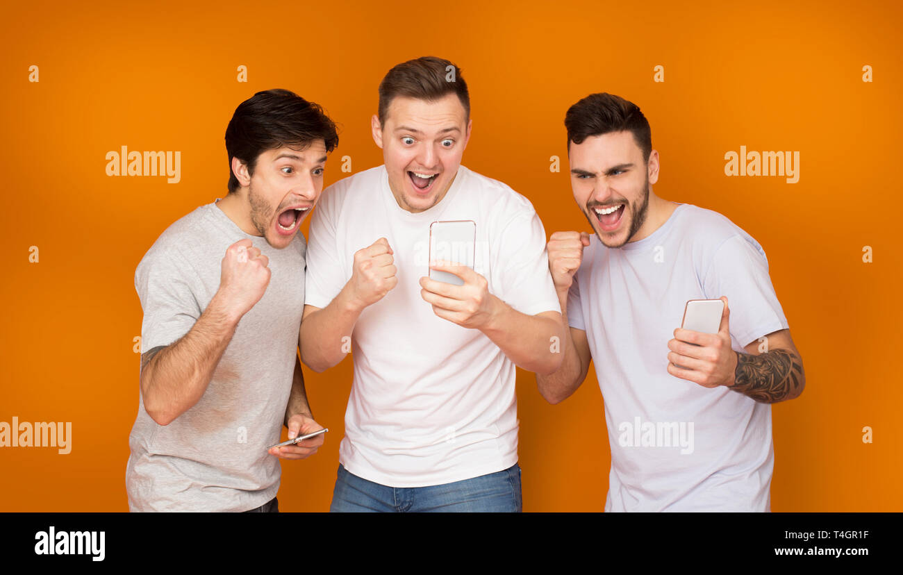 Good news. Delighted friends holding mobile phones, orange background ...