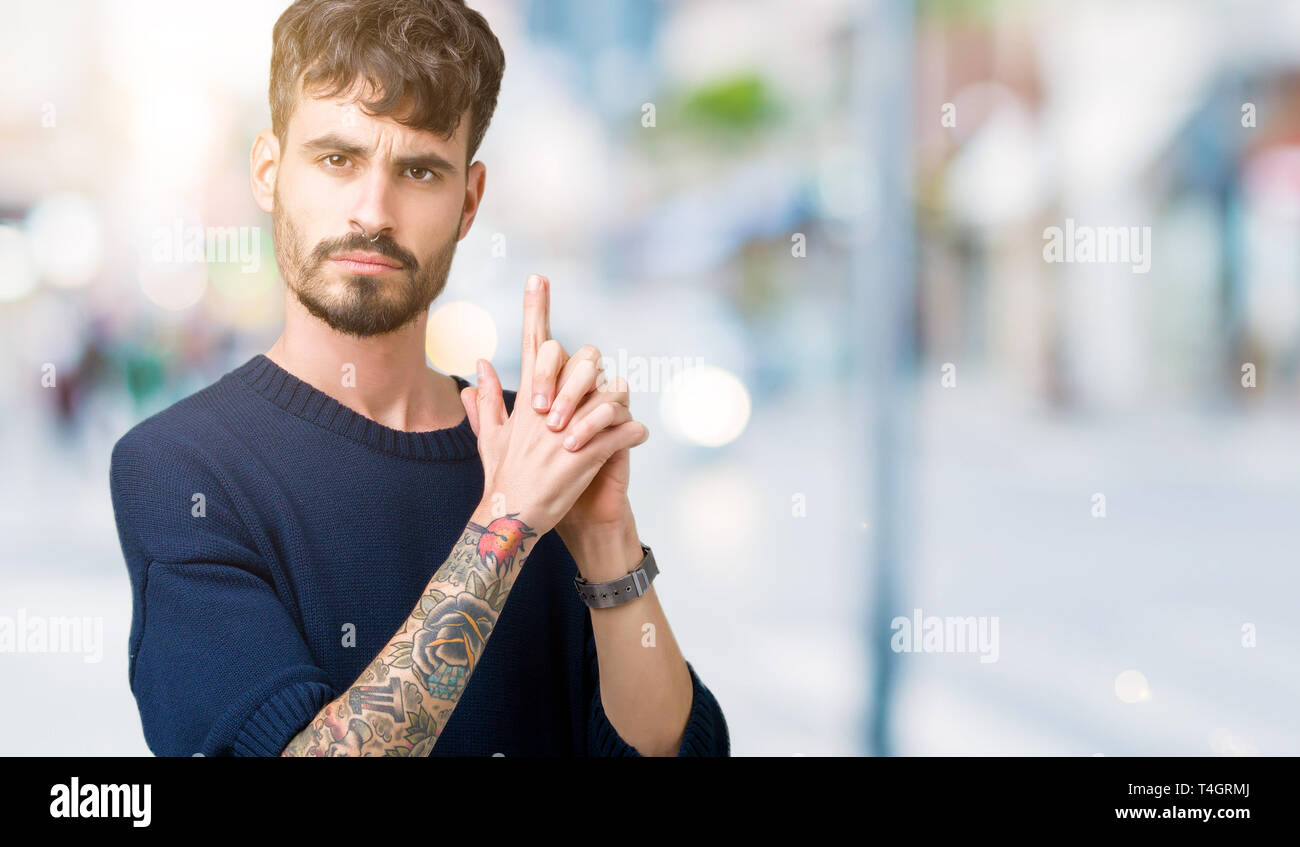 Young handsome man over isolated background Holding symbolic gun with ...