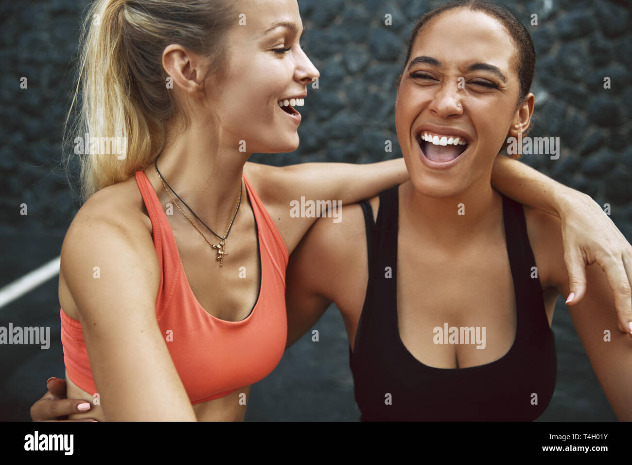 Two fit young women in sportswear laughing while sitting arm in arm in ...