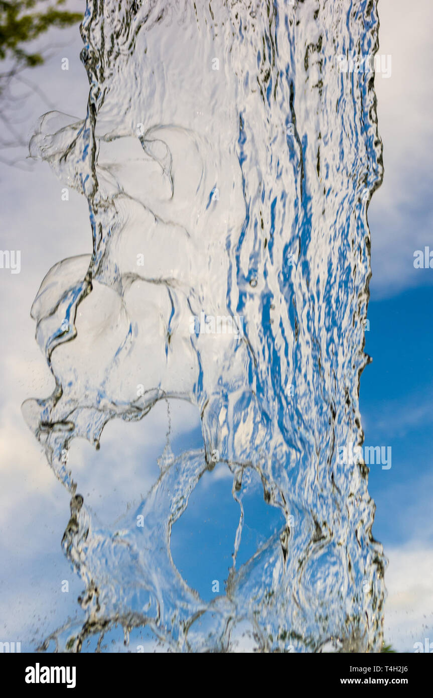 transparent falling water vertical flows against a blue sky and green ...