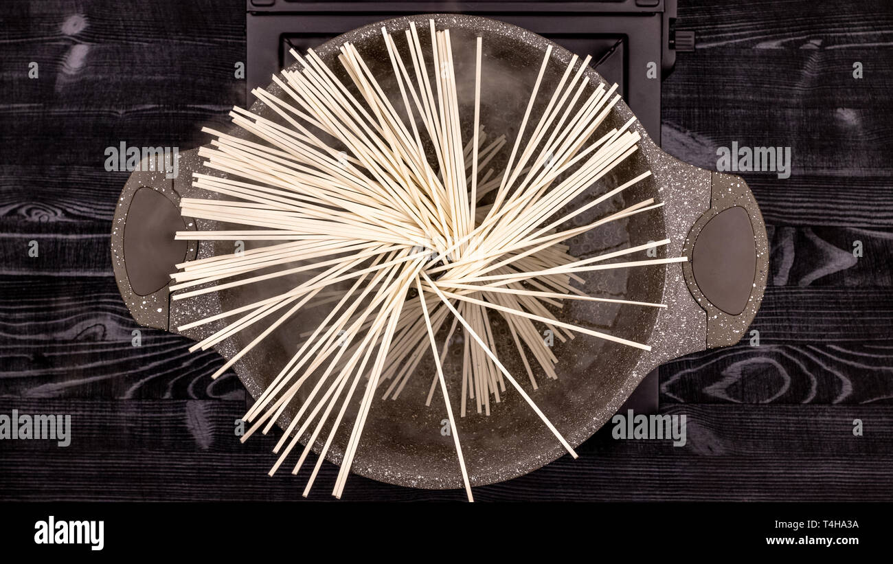 Flat noodles boiled in boiling water in a saucepan with a stone coating ...