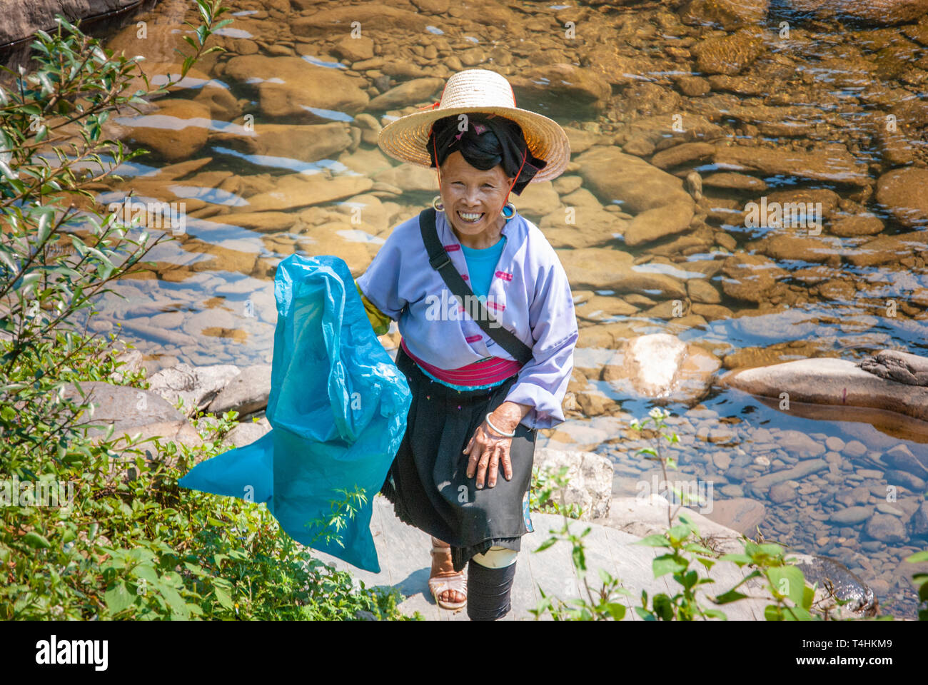 Happy old chinese woman collects trash on river bank. Asian woman ...