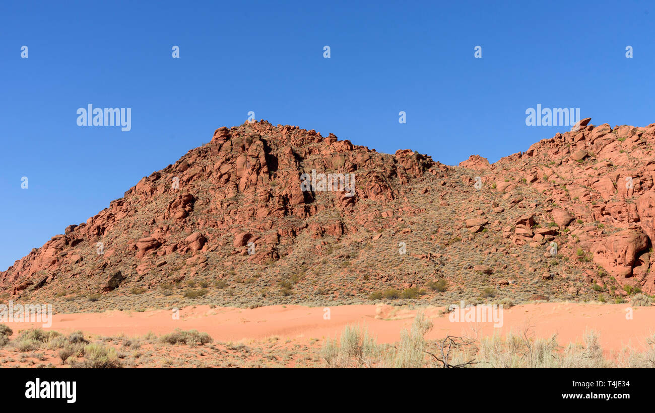 desert sand gives way to tall orange rock mountain Unser blue sky Stock ...
