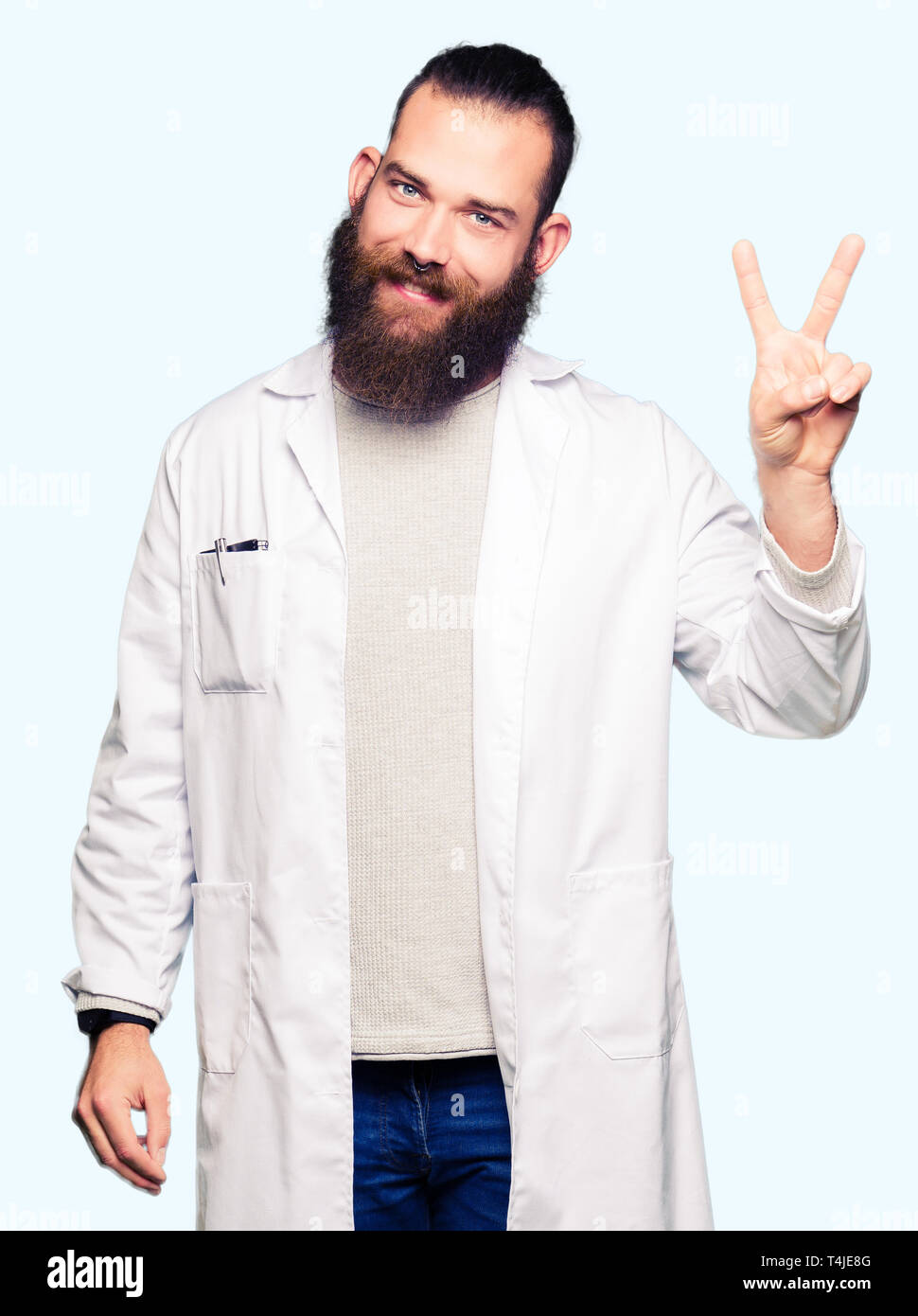 Young blond scientist man wearing white coat smiling with happy face ...