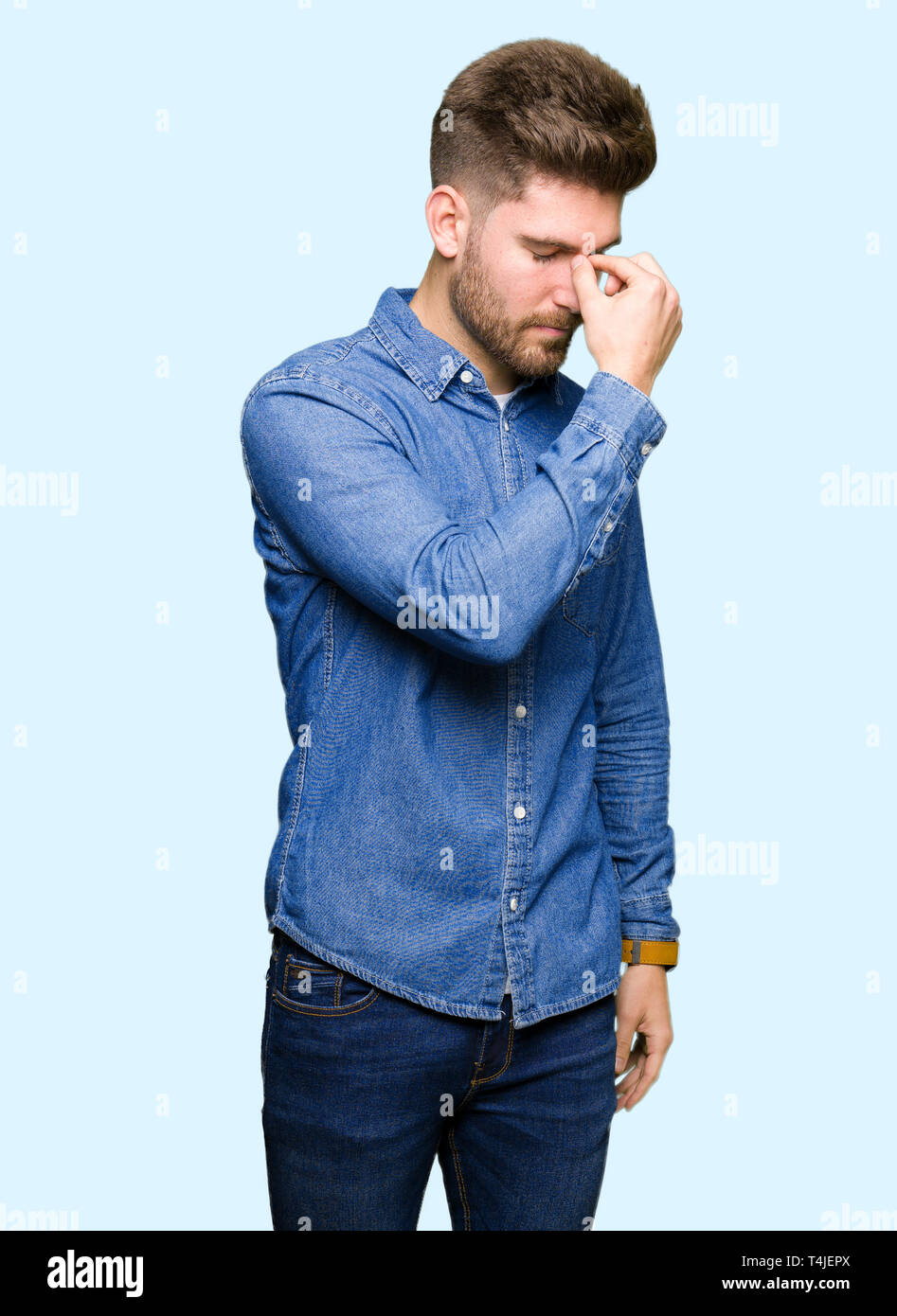 Young handsome blond man wearing casual denim shirt tired rubbing nose ...