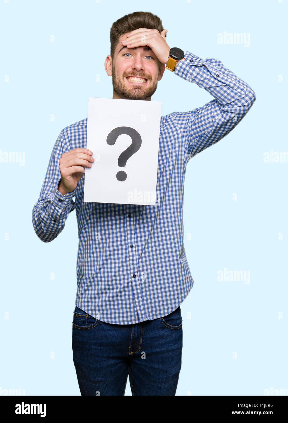 Young handsome man holding paper with question mark stressed with hand ...