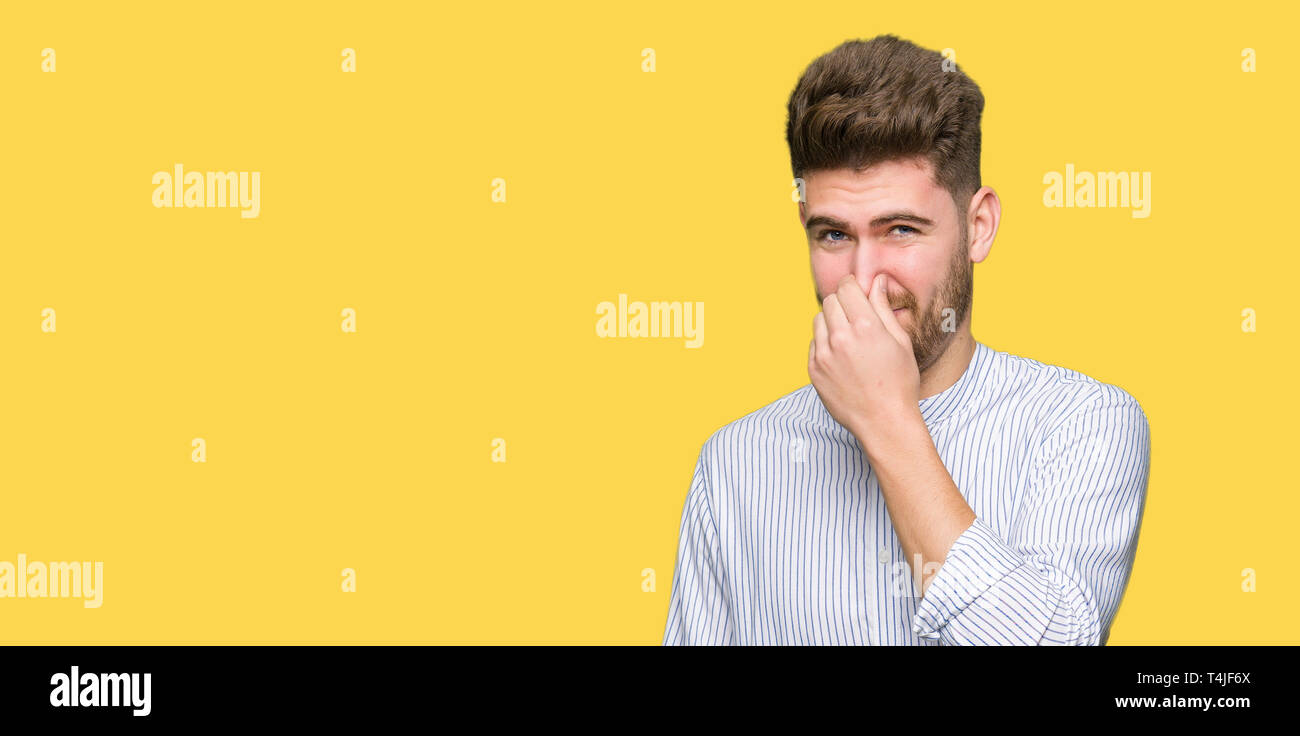 Young handsome man smelling something stinky and disgusting ...